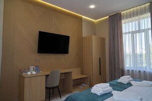 Quarto de hotel com cama, escrivaninha, cadeira, TV fixada na parede e janela com cortinas.