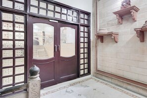 Uma porta dupla com padrão de grade, piso de azulejos e prateleira fixada na parede com um objeto decorativo.