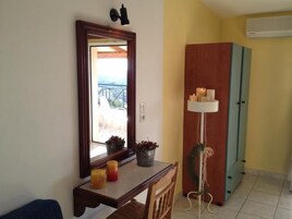 Quarto com escrivaninha de madeira, espelho, planta em vaso, luminária de chão e guarda-roupa.