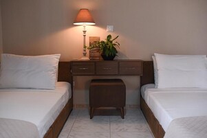 Quarto de hotel com duas camas, uma mesa de cabeceira, abajur, planta e uma pequena mesa.