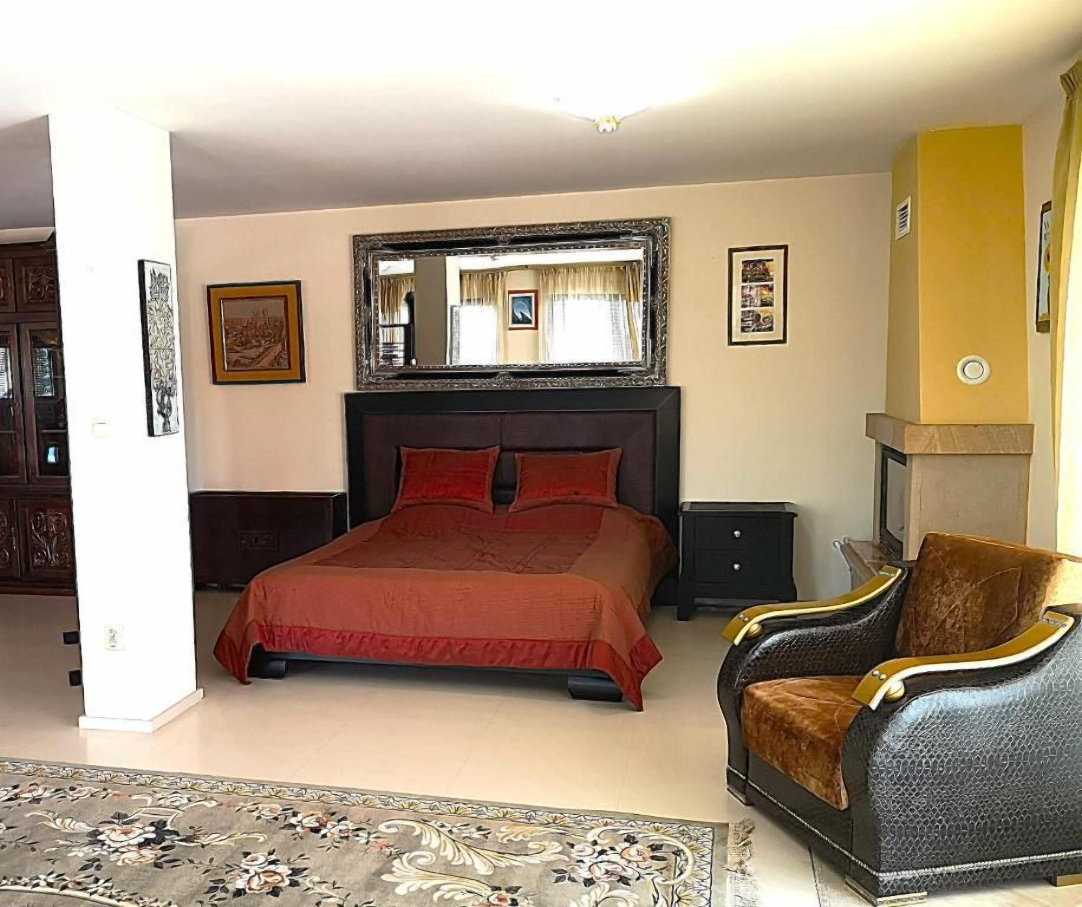 Quarto com uma cama grande, uma cadeira, um espelho e uma mesinha de cabeceira.