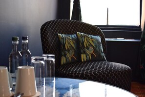 Um quarto com uma mesa redonda, uma poltrona estampada e uma janela com cortinas.