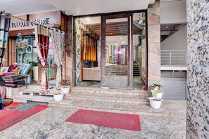 Entrada de um hotel com porta de vidro, tapete vermelho e uma placa com a inscrição 'NDOOM CENTRE'.