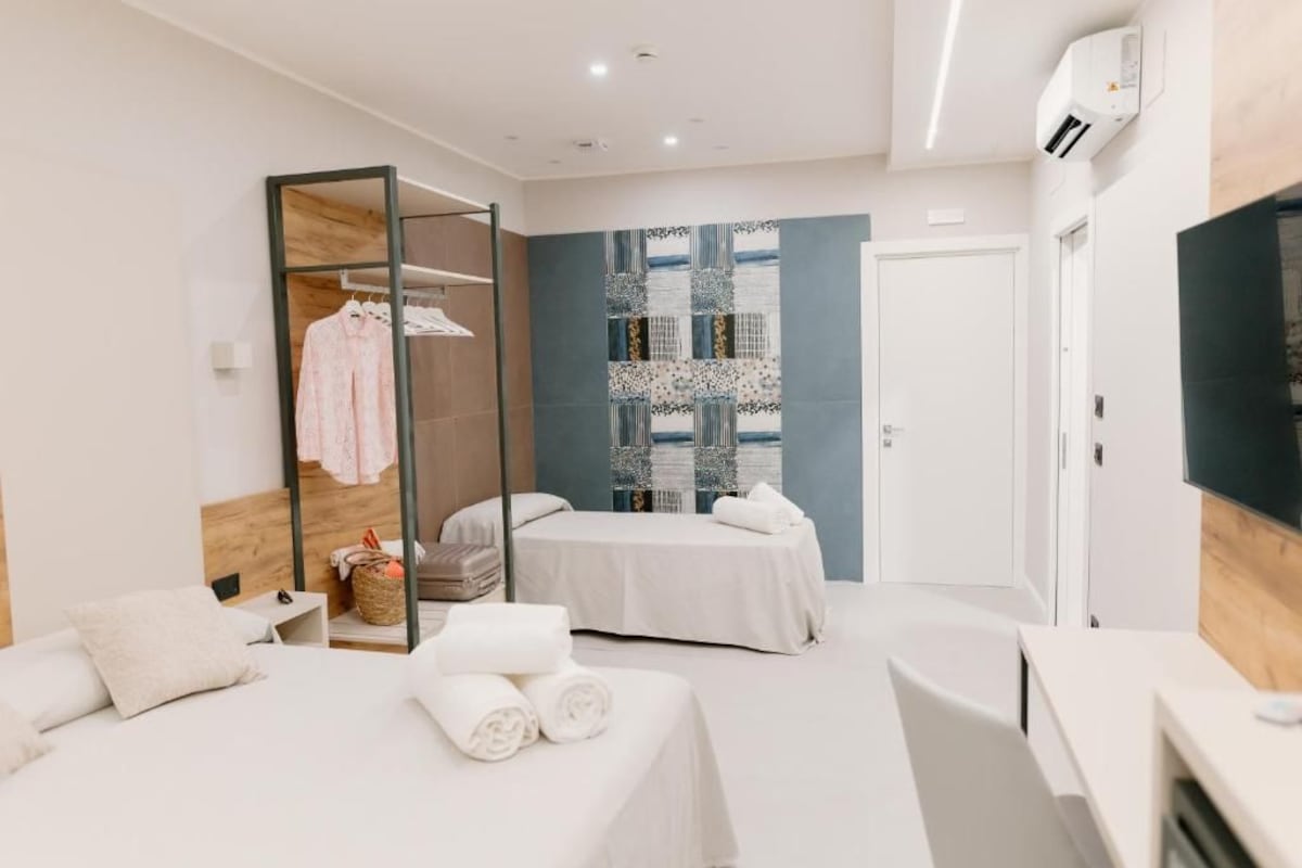 Quarto de hotel com duas camas, um espelho, uma televisão e uma parede com padrão decorativo.