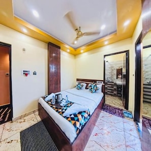Quarto de hotel com cama, ventoinha no teto, banheiro com espelho e piso revestido com azulejos.