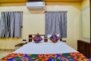 Quarto de hotel com cama, duas almofadas, ar-condicionado, cortinas e um armário de madeira.