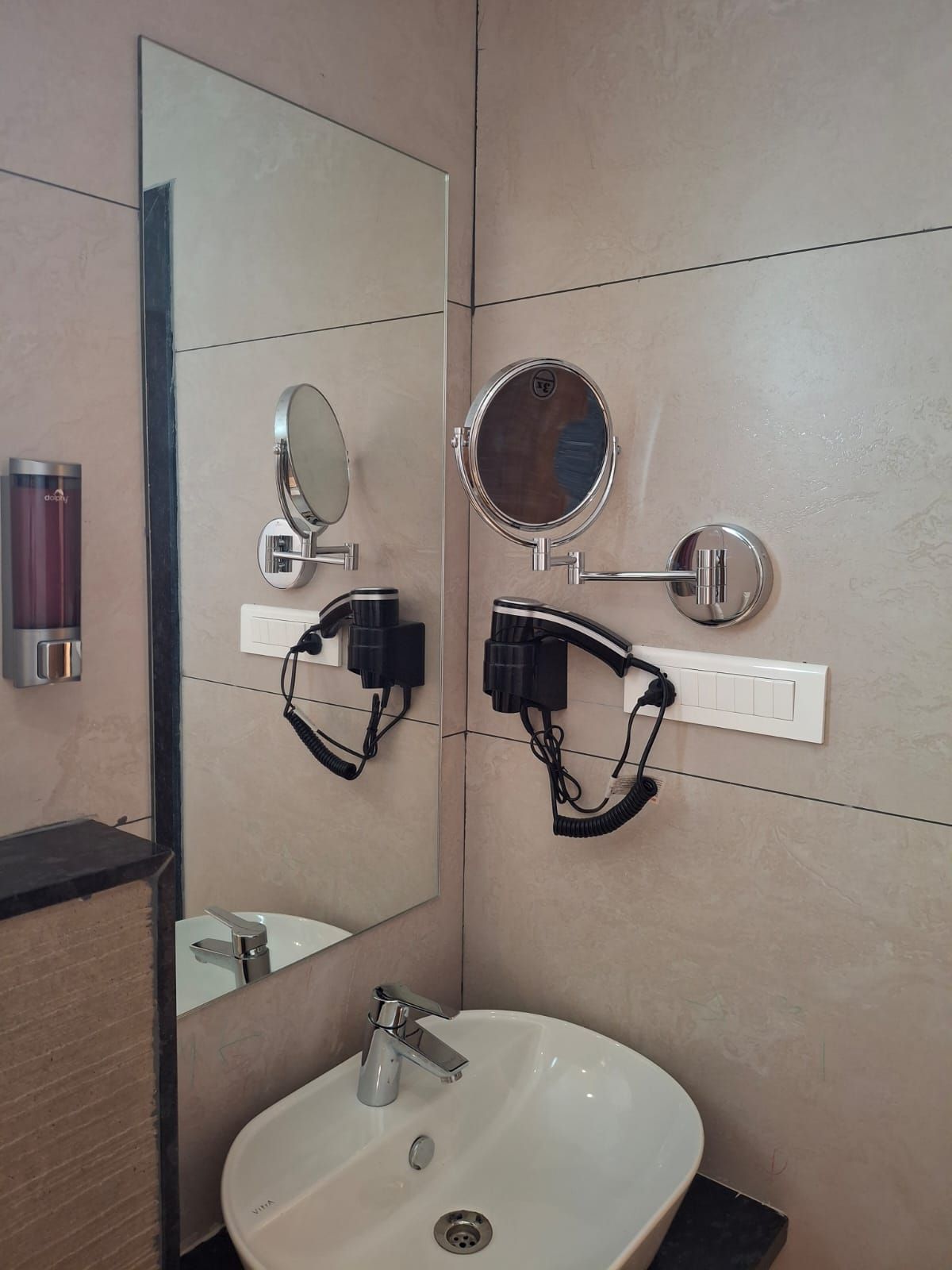 Um banheiro com um espelho grande, dois espelhos redondos, uma pia e um secador de cabelo.