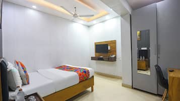 Quarto com cama, escrivaninha, guarda-roupa, ventoinha no teto e televisão na parede.