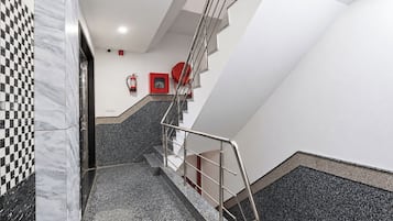 Uma escadaria com corrimão de metal, azulejos quadriculados na parede e um extintor fixado na parede.
