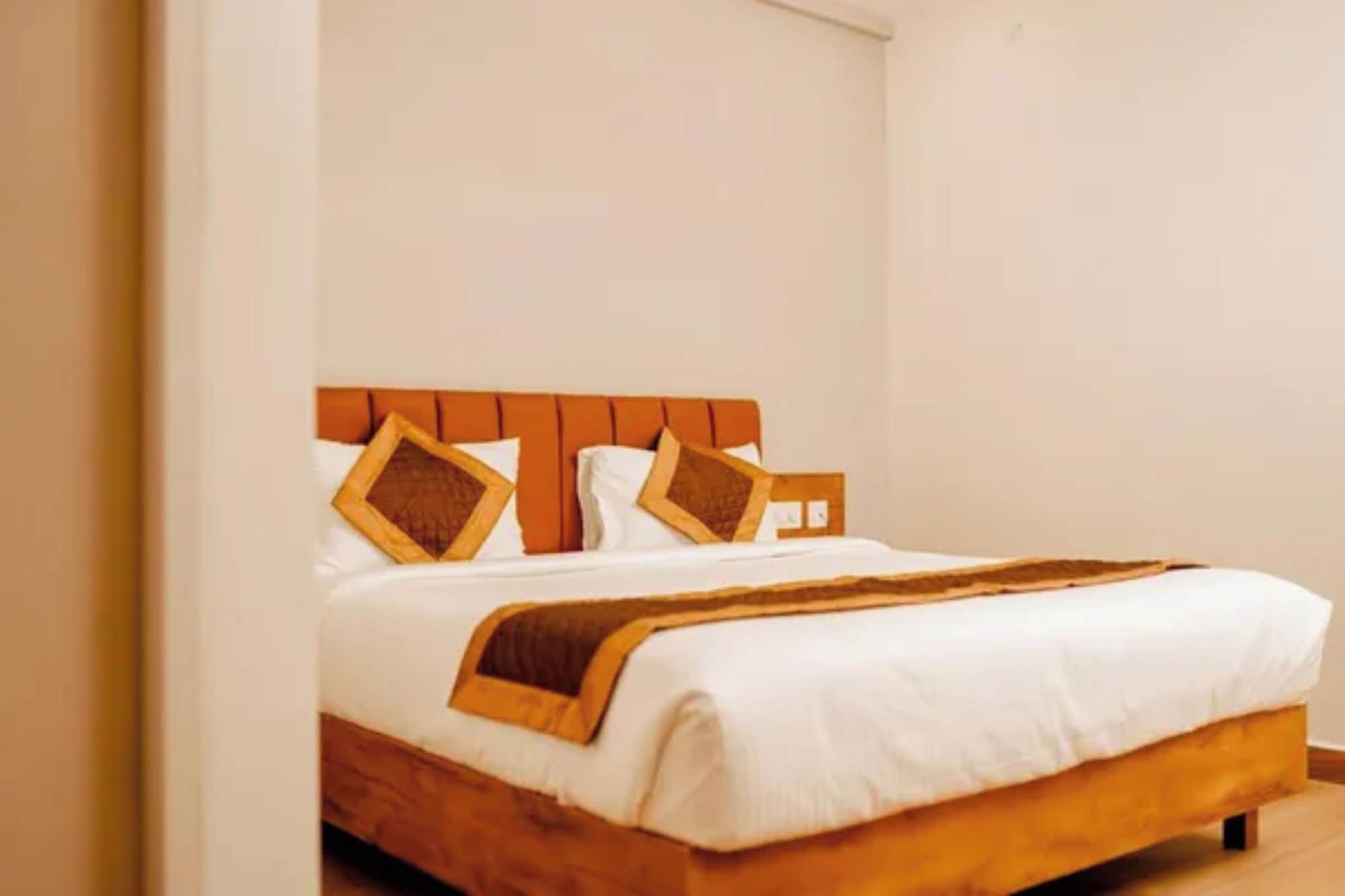 Cama de casal com cabeceira de madeira, roupa de cama branca e duas almofadas decorativas.