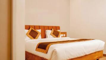 Cama de casal com cabeceira de madeira, roupa de cama branca e duas almofadas decorativas.
