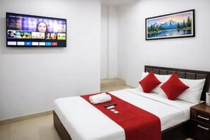 Quarto de hotel com uma cama, uma televisão fixada na parede e um quadro acima da cama.