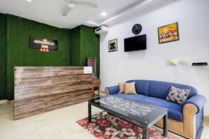 Uma área de recepção com balcão, um sofá azul, um relógio e uma televisão na parede.