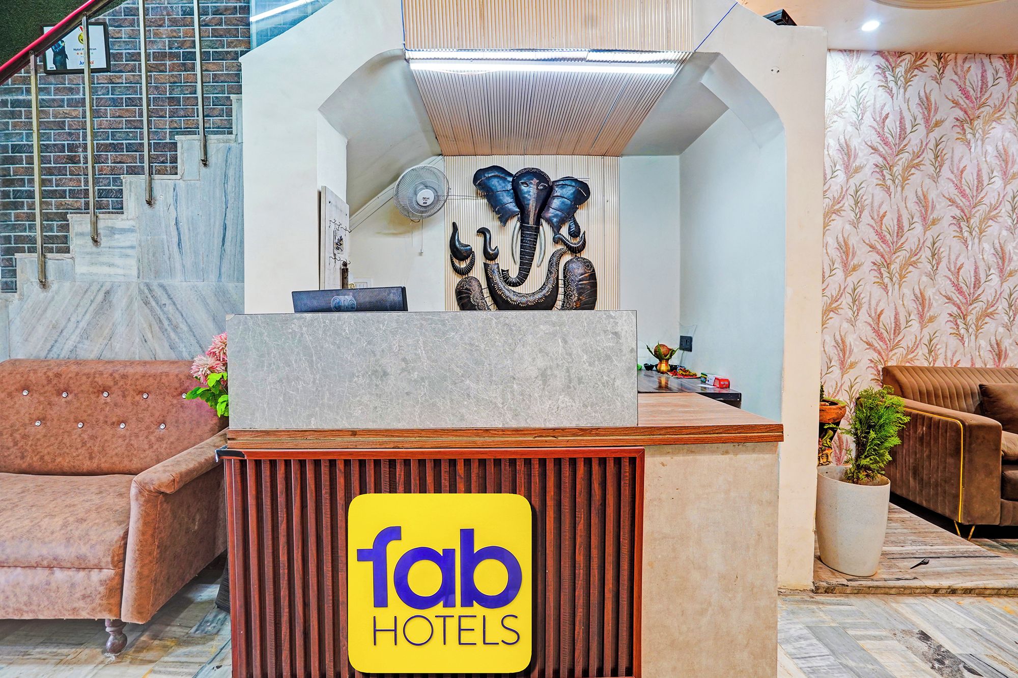 Uma área de recepção com balcão de mármore, o letreiro 'fab hotels' e uma escultura de arte moderna.