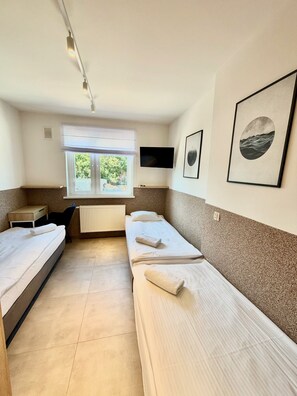 Quarto de hotel com duas camas, uma janela, televisão de tela plana e obras de arte nas paredes.