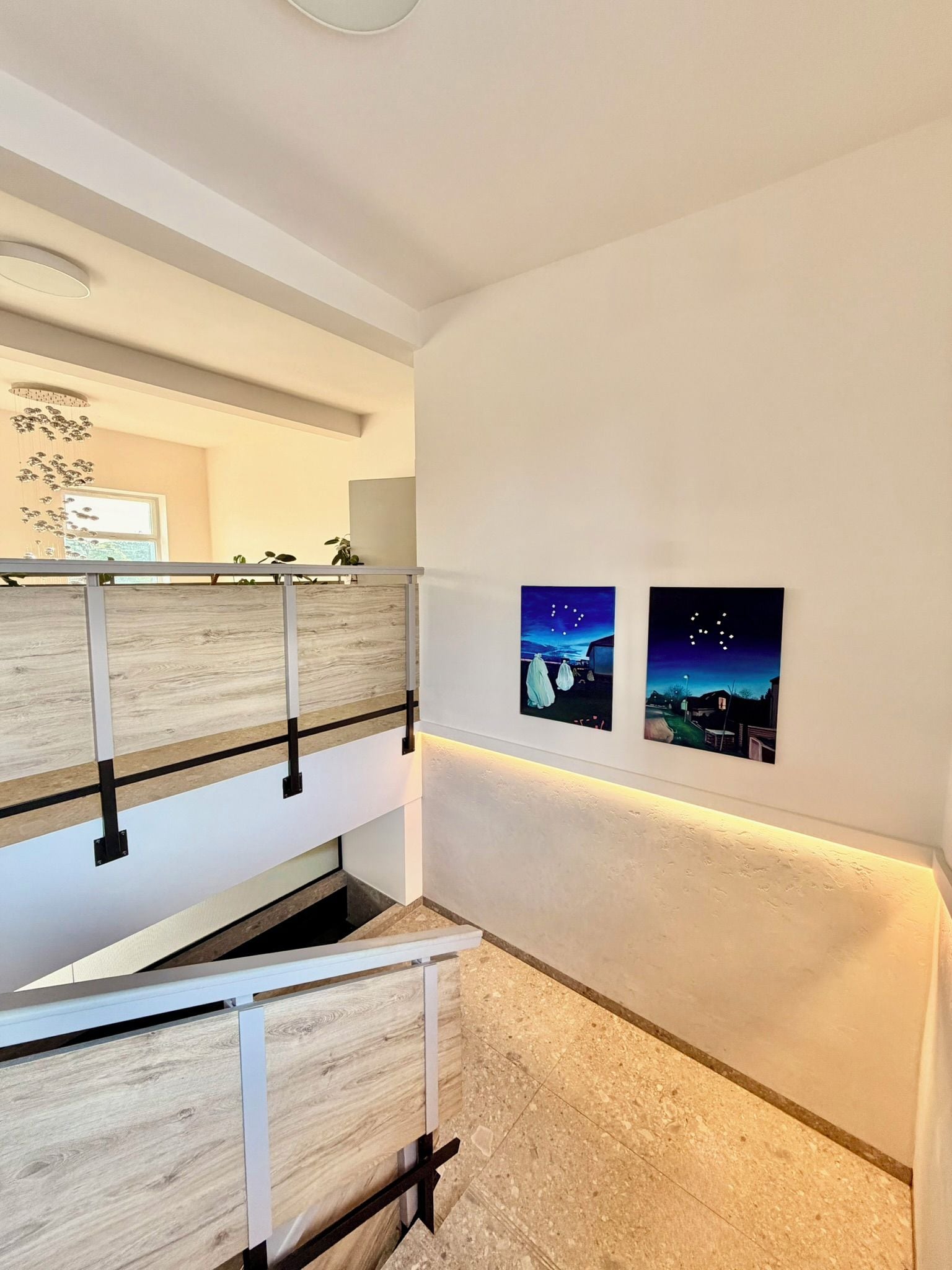 Interior moderno com escada, painéis de madeira e obras de arte nas paredes.