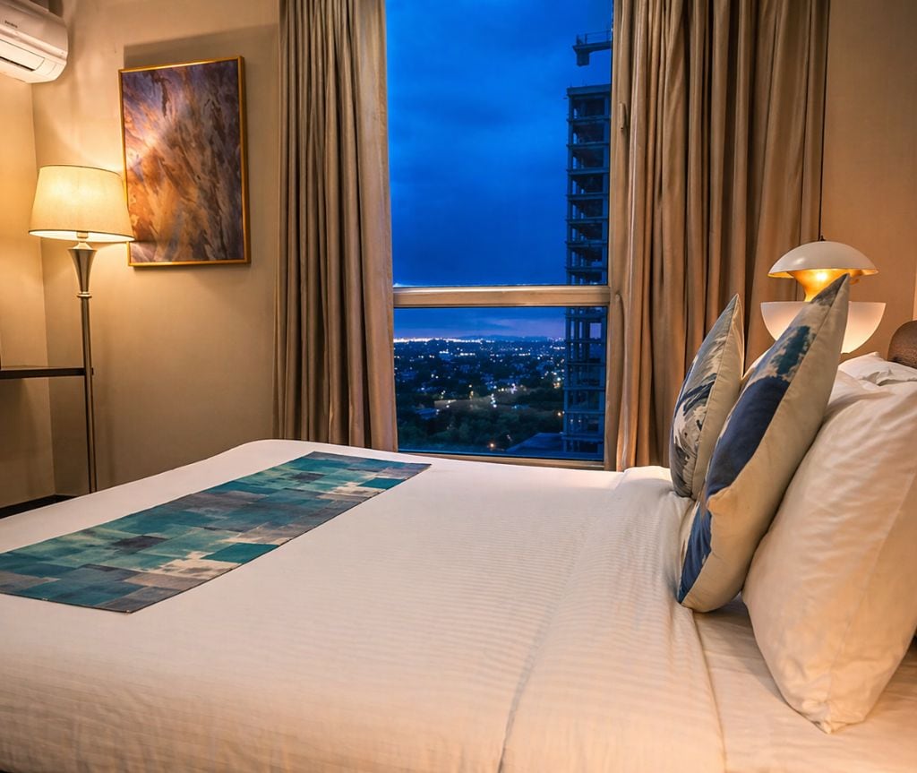 Quarto de hotel com uma cama grande, vista da cidade pela janela e um quadro na parede.