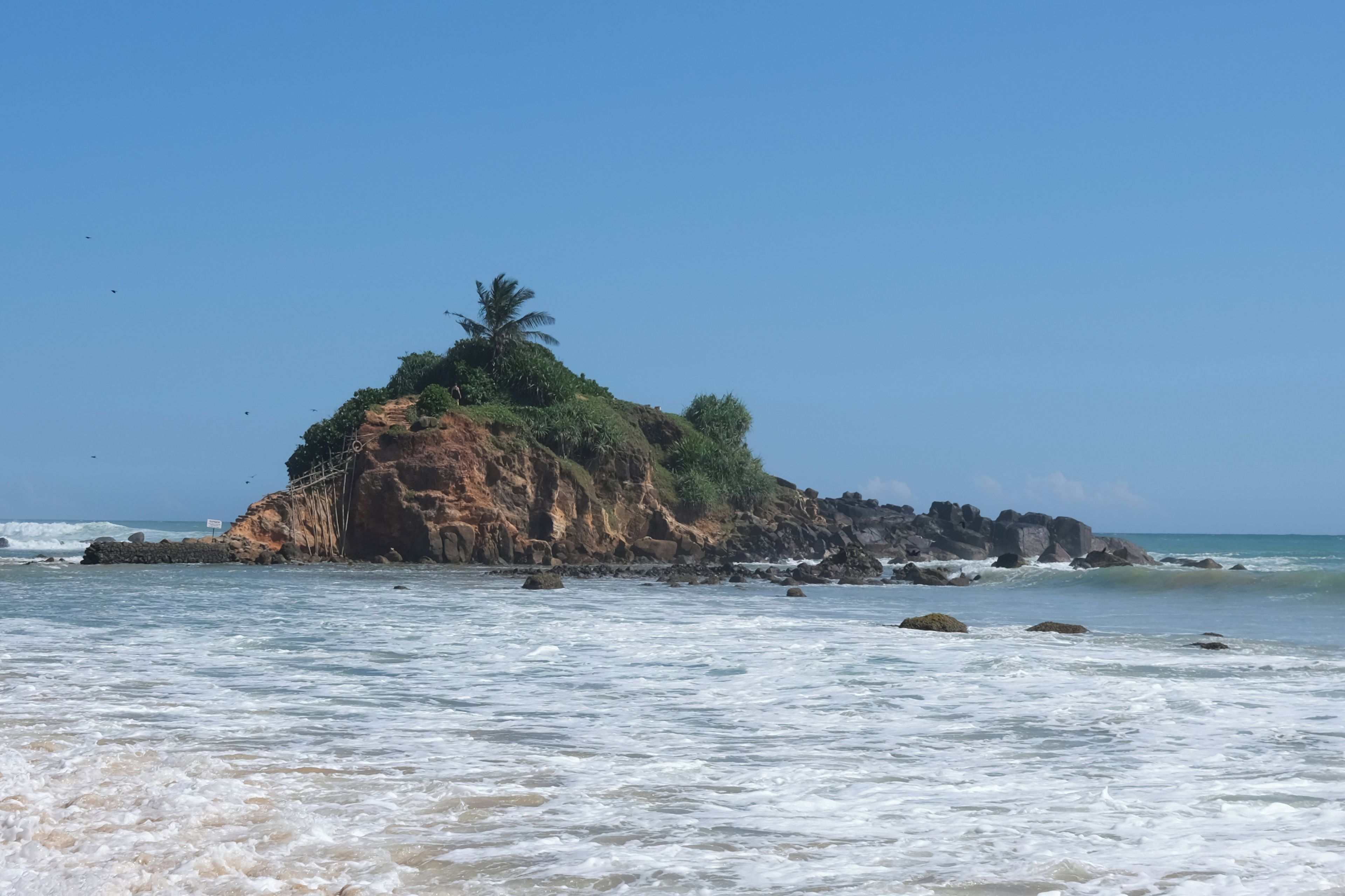 Uma ilha rochosa com vegetação e céu claro.