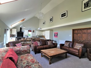 Uma sala de estar ampla, com lareira, sofás de couro e uma mesa de centro de madeira.