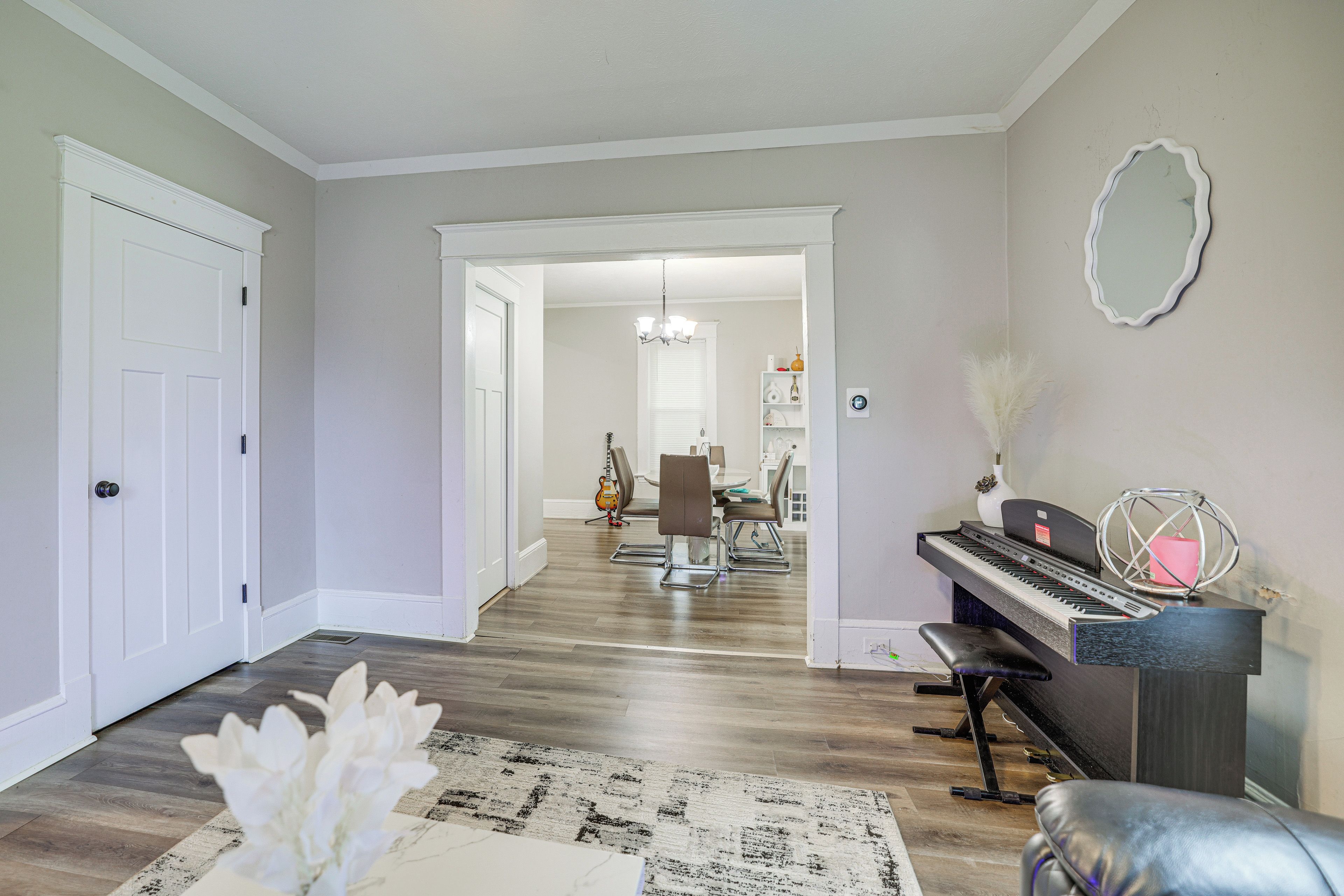 Sala de estar ampla com um piano, área de jantar ao fundo e um corredor que dá para outro cômodo.