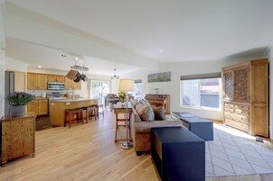 Ampla sala de estar com cozinha, piso de madeira e uma grande janela.