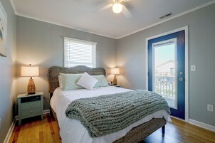 Quarto com cama, duas mesas de cabeceira com abajures, um ventilador de teto e uma porta que dá para uma varanda.