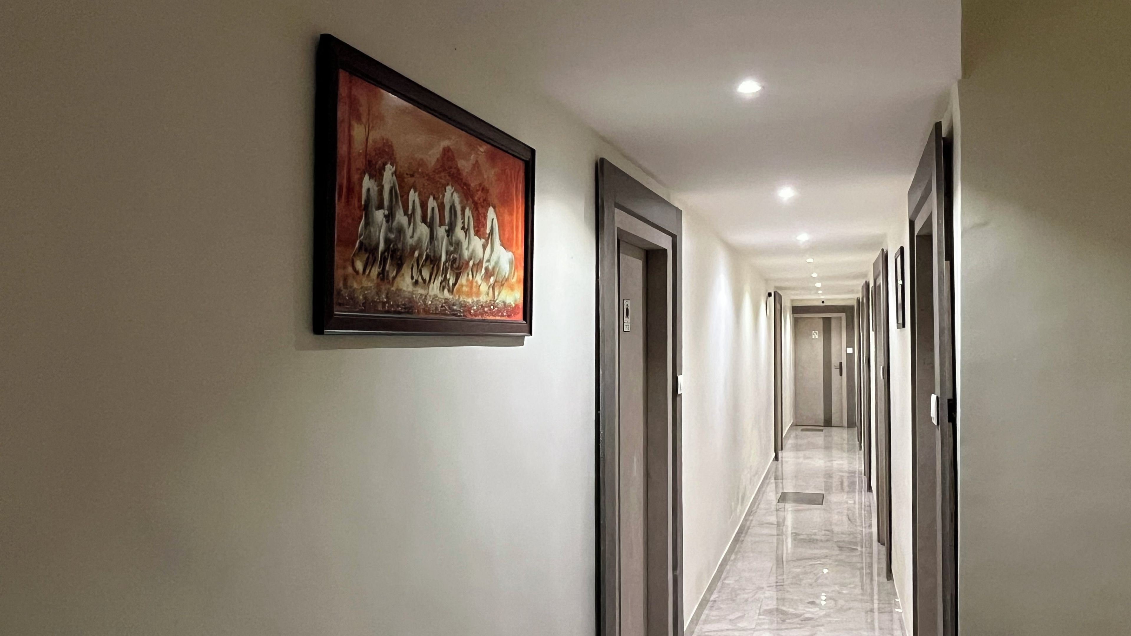 Corredor com portas em ambos os lados, uma obra de arte emoldurada na parede esquerda e teto com iluminação embutida.