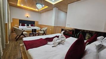 Quarto de hotel com teto de madeira, um lustre, cama com edredom branco e almofadas vermelhas, cabeceira de madeira e uma pequena mesa com uma cadeira.