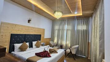Quarto de hotel com teto de madeira, uma cama grande com travesseiros, um candelabro e vista do exterior através de cortinas.
