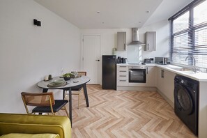 Cozinha compacta com área de refeições, máquina de lavar e janela com persianas.