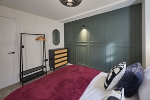 Quarto com cama, guarda-roupa, espelho e cabideiro.