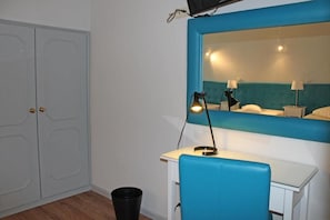 Quarto com escrivaninha, cadeira, espelho e televisão.