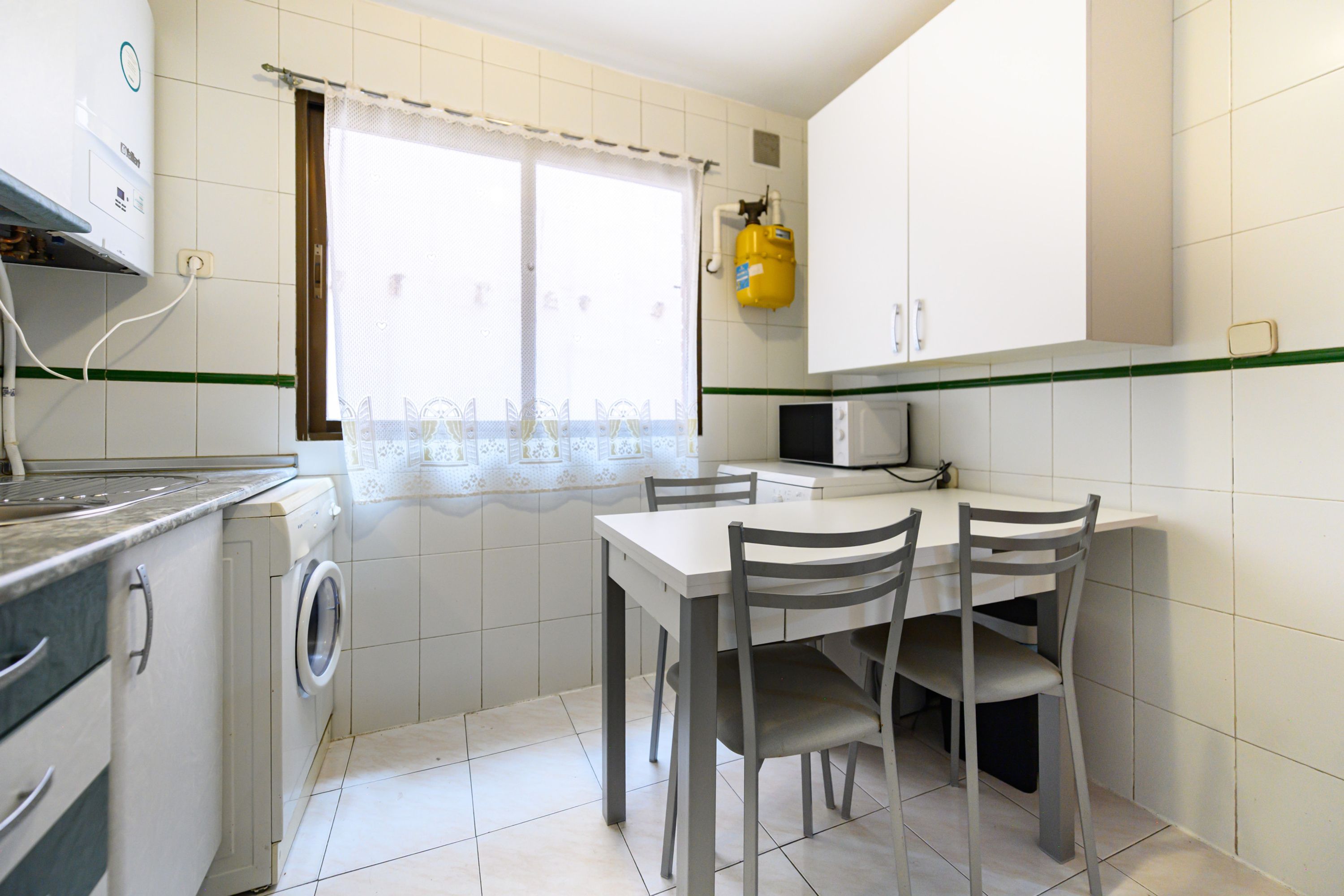 Cozinha compacta equipada com máquina de lavar, micro-ondas e espaço de refeições com cadeiras.
