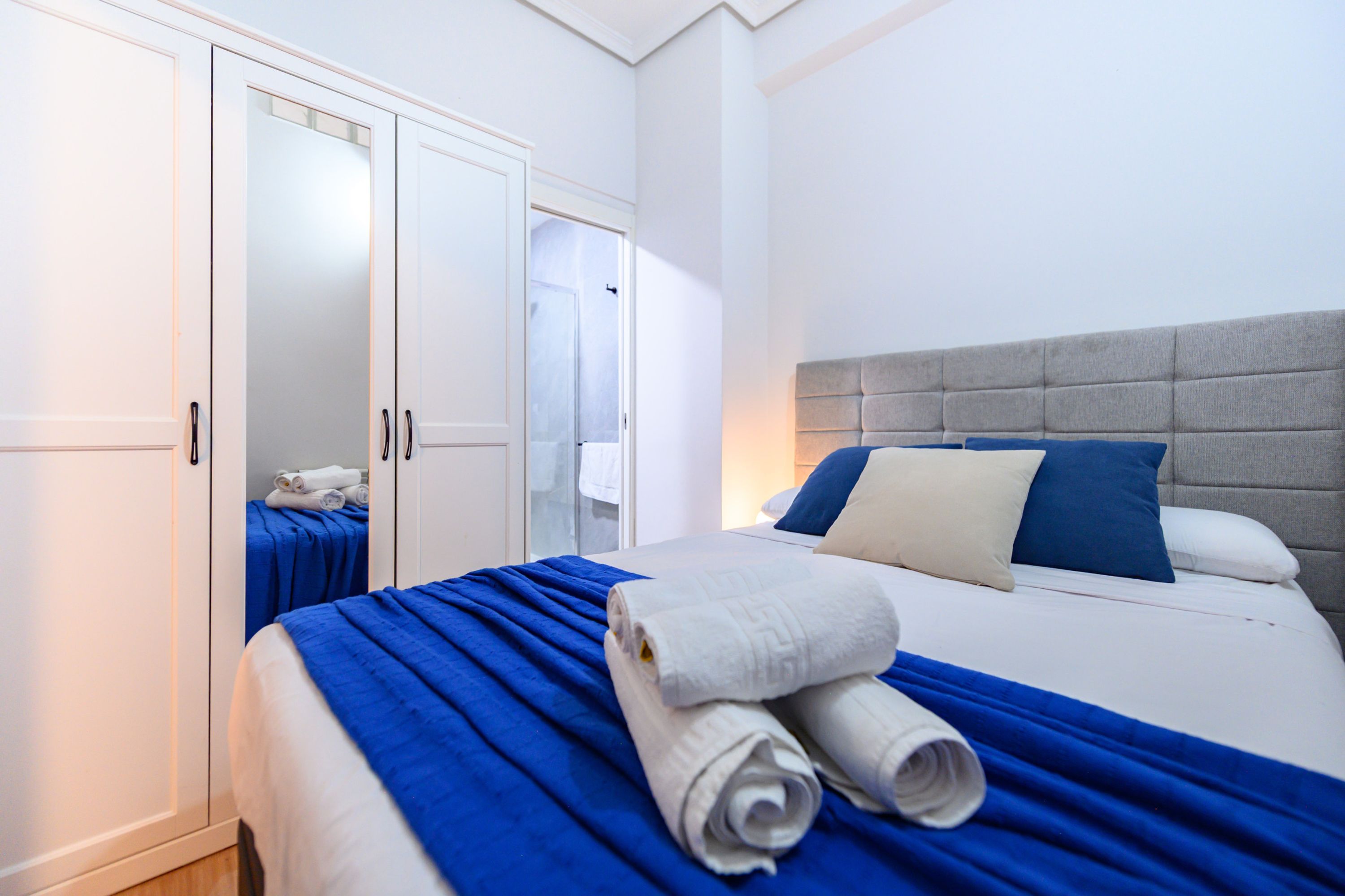 Quarto de hotel com uma cama, um guarda-roupa e um banheiro visível por uma porta aberta.