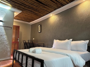Quarto de hotel com cama, mesas de cabeceira, teto de madeira e porta.