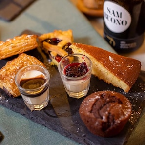 Um prato de sobremesas com doces, uma fatia de bolo e dois pequenos copos de uma bebida cremosa.
