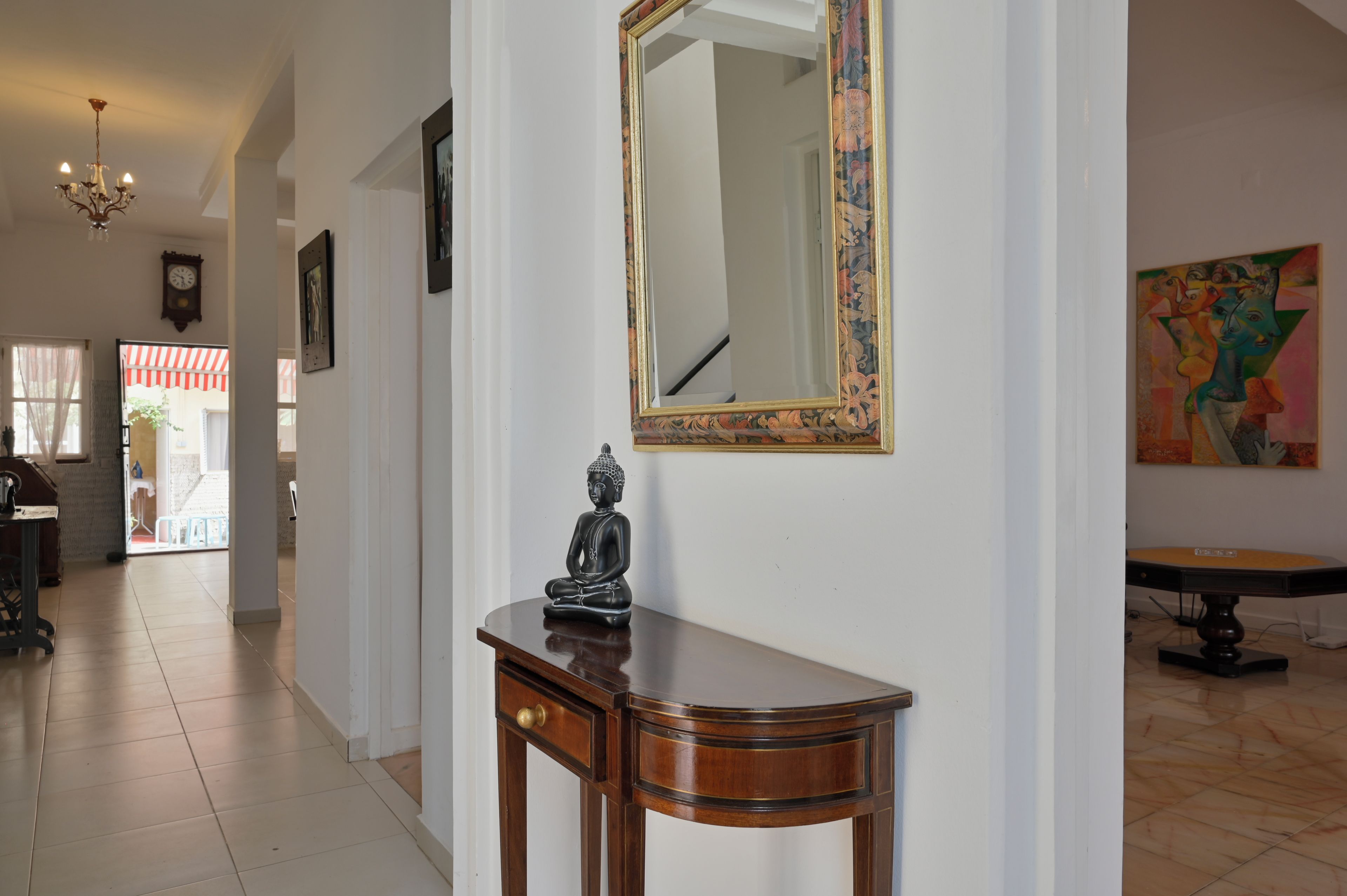 Um corredor com um aparador de madeira, um espelho com moldura decorativa e uma estátua de Buda.