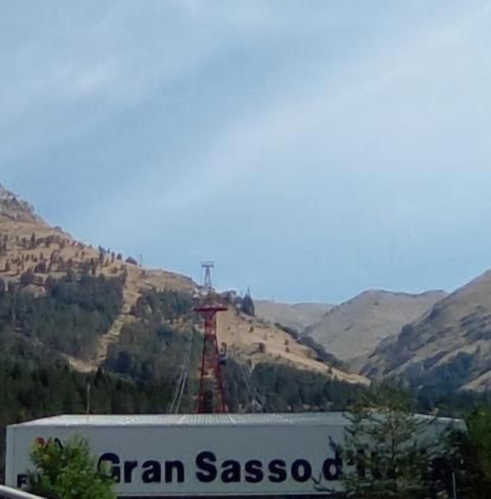 Paisagem montanhosa com um grande edifício branco identificado como 'Gran Sasso'.