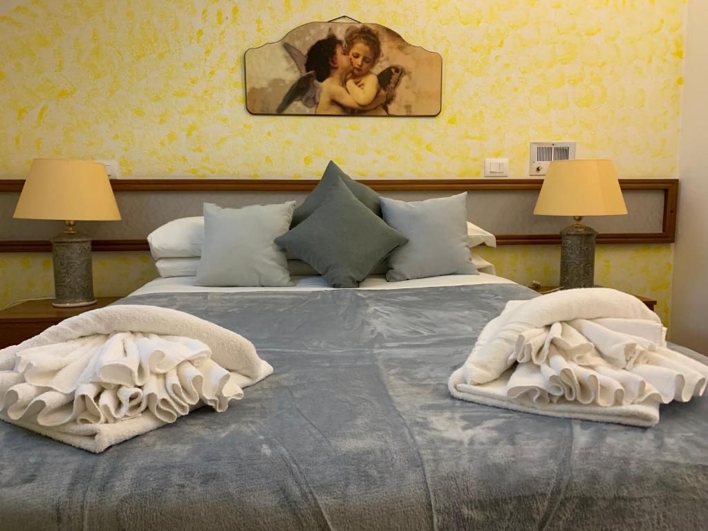 Quarto de hotel com cama, almofadas, um quadro na parede e duas luminárias.