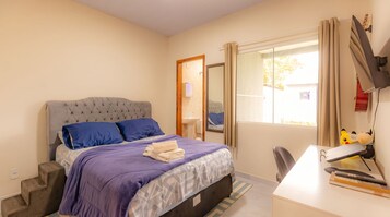 Quarto com cama, mesa de cabeceira, cadeira e janela com cortinas.