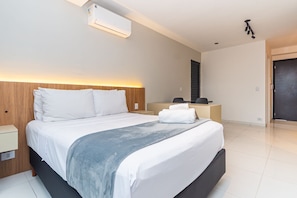 Quarto de hotel moderno com cama grande, mesas de cabeceira, escrivaninha e guarda-roupa.