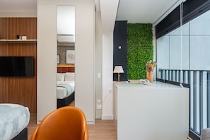 Quarto de hotel moderno com uma cama, escrivaninha, poltrona, televisão e varanda com parede verde.