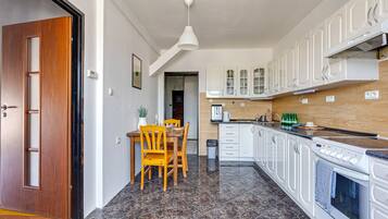 Uma cozinha moderna com armários brancos, uma área de refeições com cadeiras de madeira e piso de azulejos pretos.