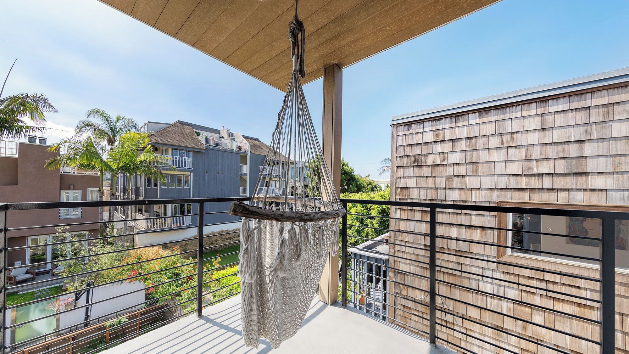 Varanda com cadeira suspensa, quadra de basquete e vista para edifícios vizinhos.