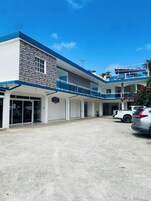 Um edifício de vários andares com área de estacionamento coberta, um letreiro de restaurante visível e uma caminhonete branca estacionada na frente.