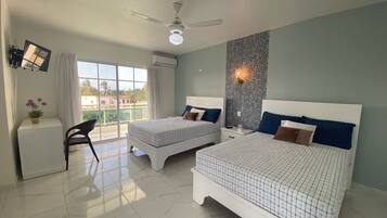 Quarto com duas camas, ventoinha no teto, janela com cortinas e vista para prédios.