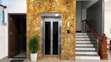 Interior com balcão de recepção, planta em vaso, escada e elevador.