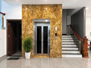 Interior com balcão de recepção, planta em vaso, escada e elevador.