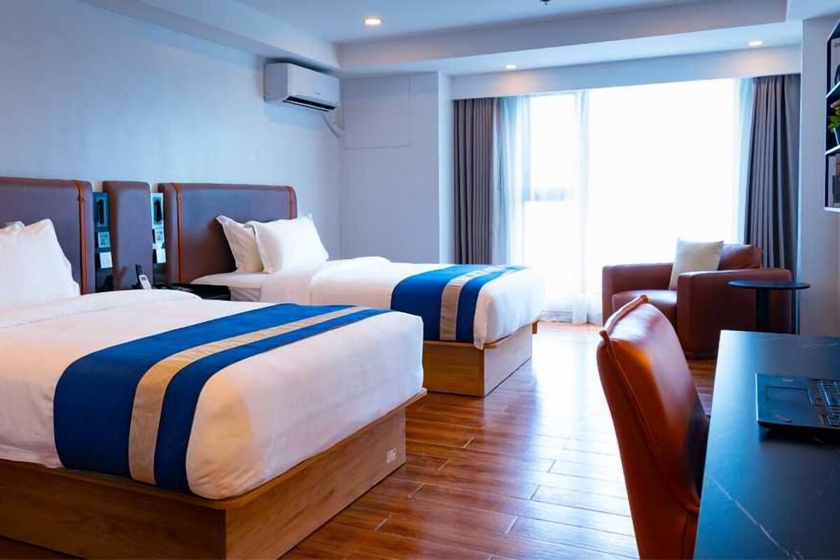 Quarto de hotel com duas camas, uma escrivaninha e uma cadeira.