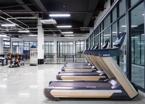 Academia com esteiras, equipamentos de ginástica e amplas janelas.